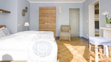 Quarto com uma cama, uma cadeira de vime, uma mesinha e um guarda-roupa de madeira.