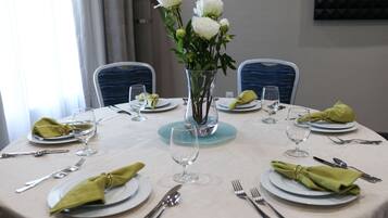 Mesa de jantar posta para quatro com pratos brancos, guardanapos verdes e um vaso transparente com flores brancas.
