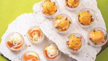 Diversos pratos de pequeno-almoço em copos transparentes, incluindo ovos Benedict e omeletes, dispostos sobre uma superfície branca com textura.