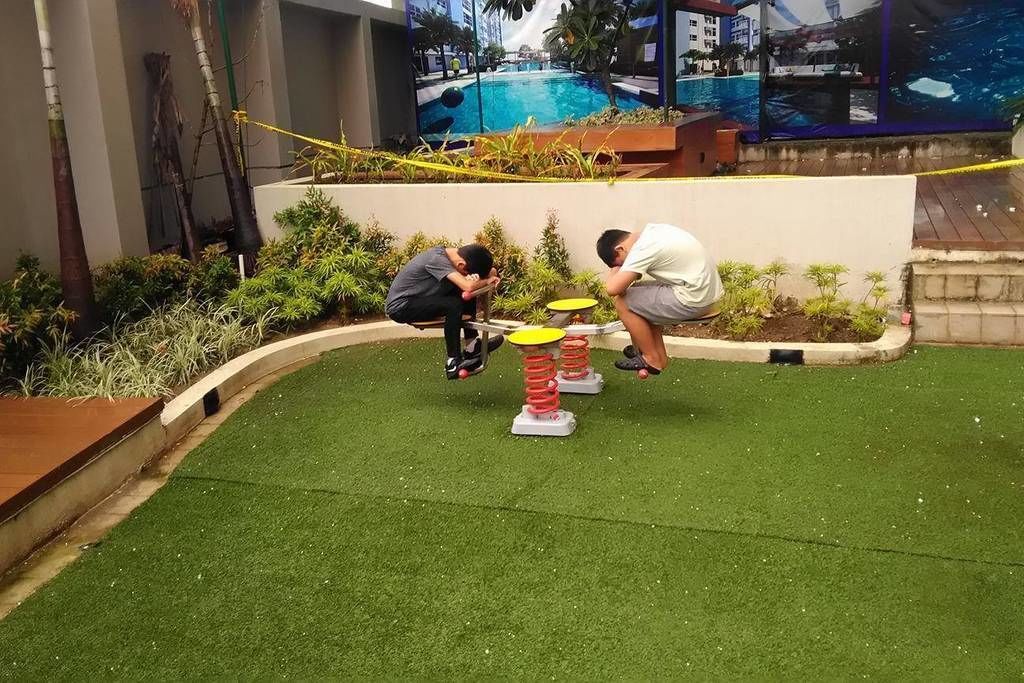 Duas pessoas jogando um jogo em grama sintética, com piscina e edifícios ao fundo.