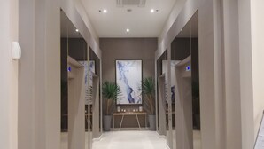 Um corredor com piso de mármore, ladeado por portas de vidro e uma obra de arte central.