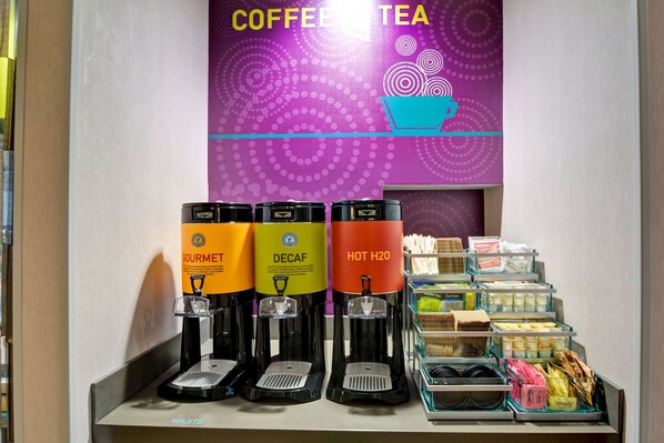 Estação de café e chá com três máquinas de café identificadas como 'Gourmet', 'Descafeinado' e 'Água Quente'. Há também diversos sachês de chá e recipientes no lado direito.