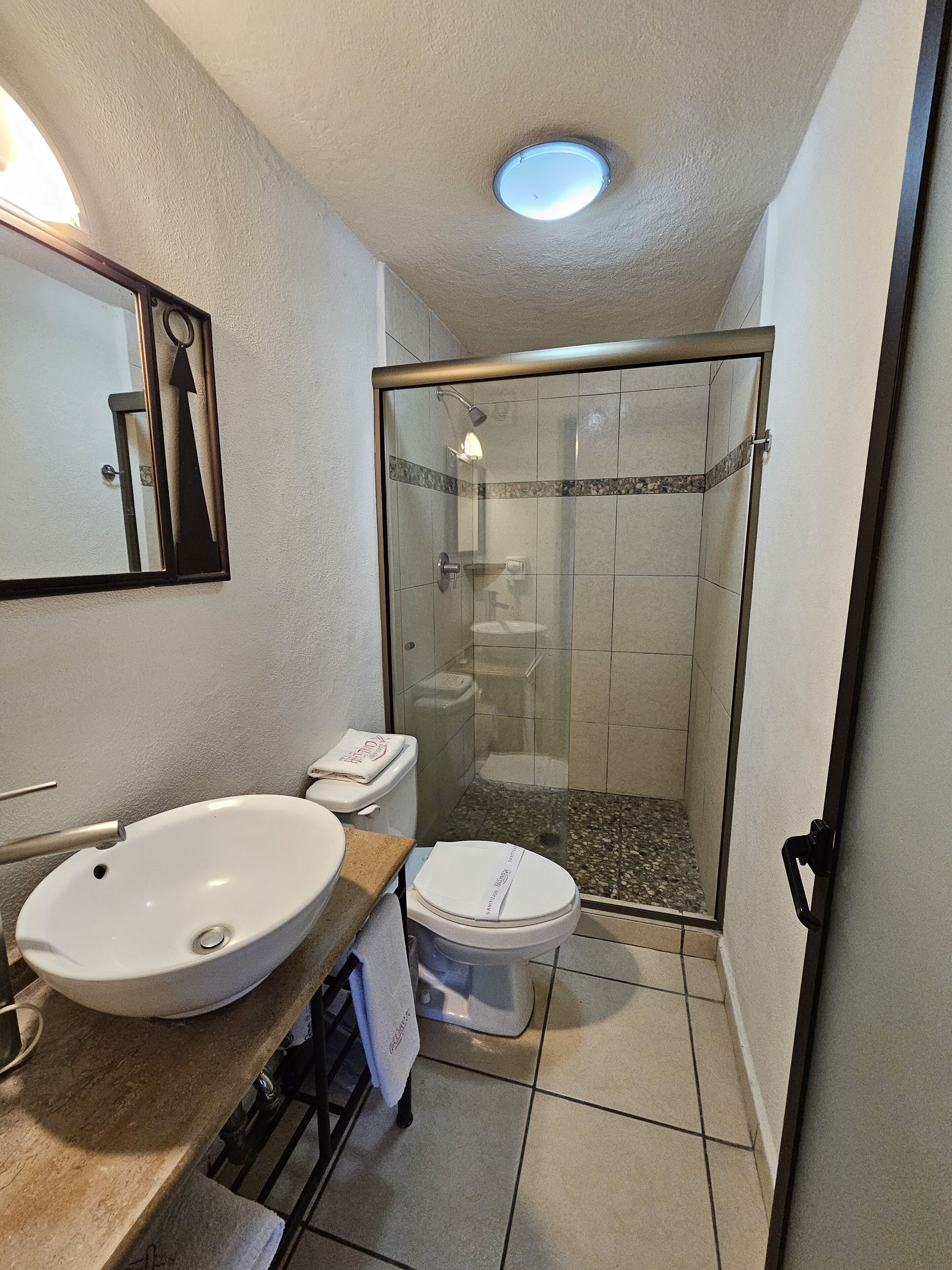 Uma casa de banho com cabine de duche em vidro, uma pia e sanita.