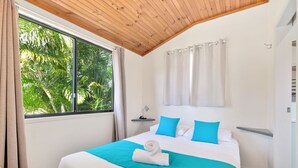 Quarto de hotel com uma cama grande, teto de madeira, janela com cortinas e vista para o verde lá fora.
