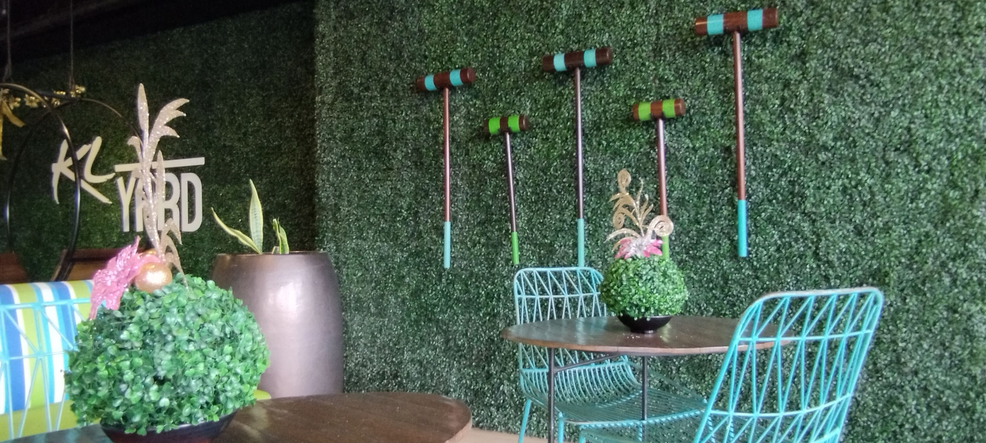 Uma área de refeições com parede verde, cadeiras de metal e uma mesa.
