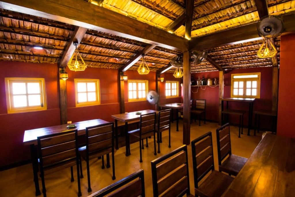 Um restaurante com mesas e bancos de madeira, telhado de palha e luminárias pendentes.