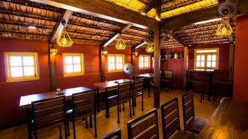Um restaurante com mesas e bancos de madeira, telhado de palha e luminárias pendentes.