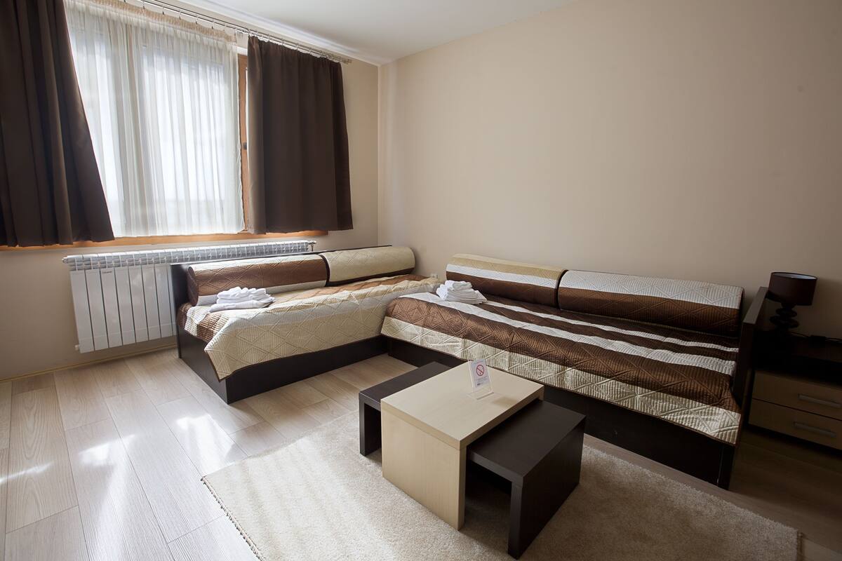 Quarto moderno com uma cama grande, uma mesa de cabeceira, um radiador e uma janela com cortinas.
