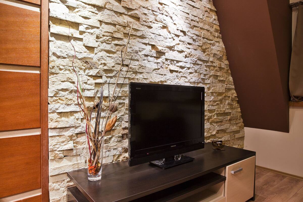 Uma sala de estar moderna com parede de pedra, lambris de madeira, uma TV de tela plana e um armário de madeira.