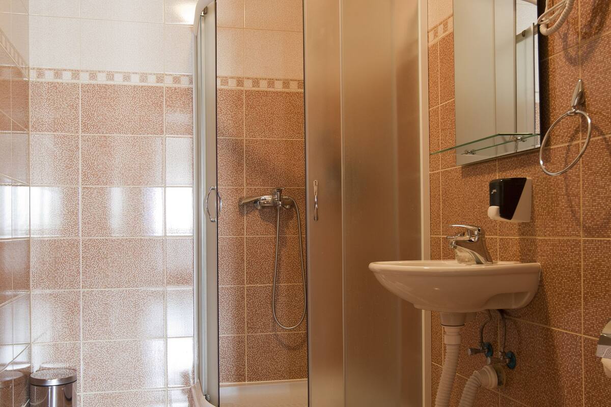 Casa de banho com chuveiro de vidro, lavatório e sanita.