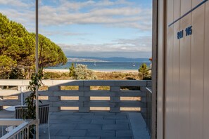 Uma varanda com vista para o mar, uma praia e um horizonte urbano distante.