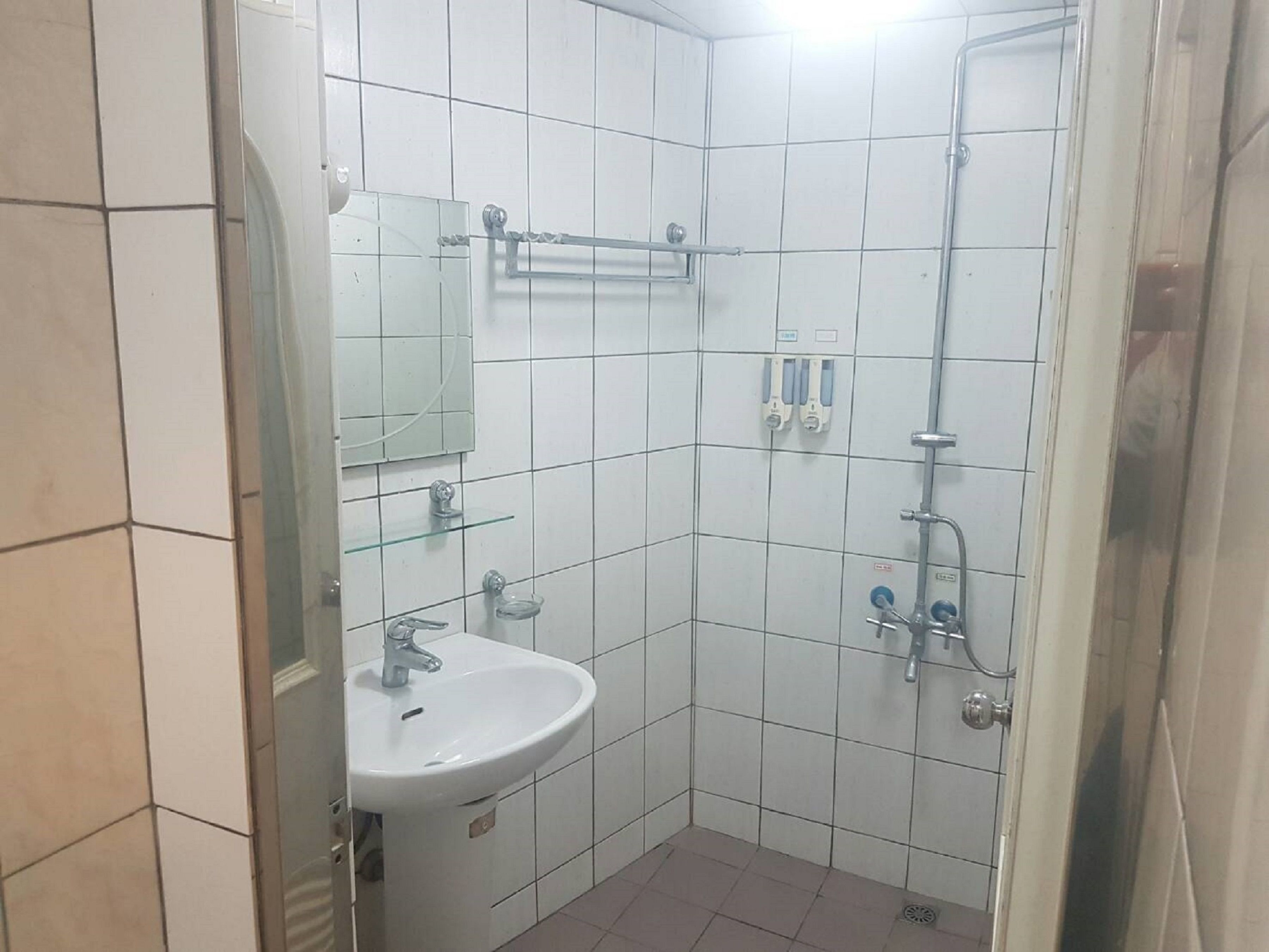 Um banheiro pequeno com azulejos, pia, espelho e chuveiro.