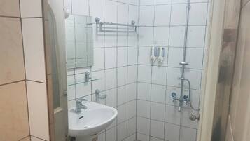 Um banheiro pequeno com azulejos, pia, espelho e chuveiro.