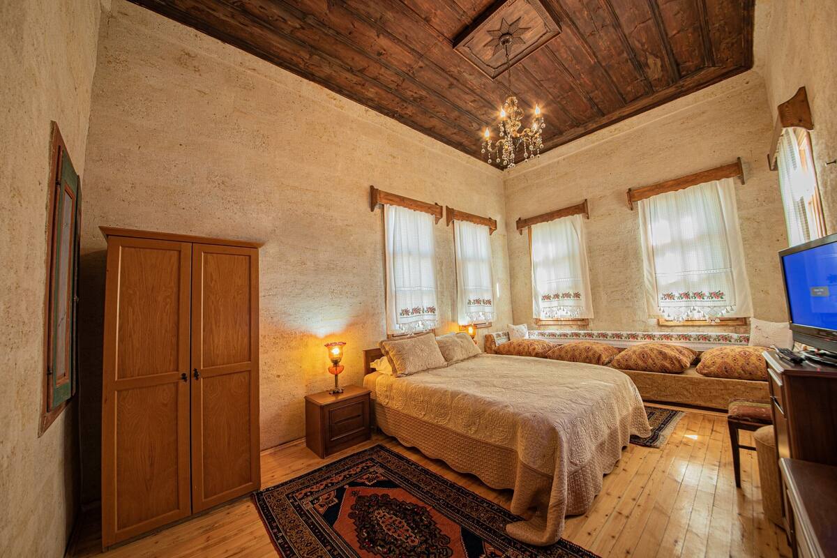 Quarto com teto de madeira, uma cama grande, mesa de cabeceira, televisão e guarda-roupa.