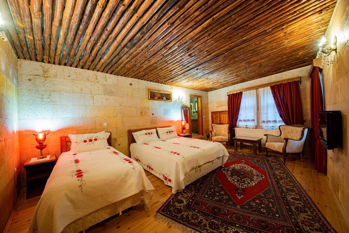 Quarto com duas camas, teto de madeira, tapete vermelho e uma cadeira.