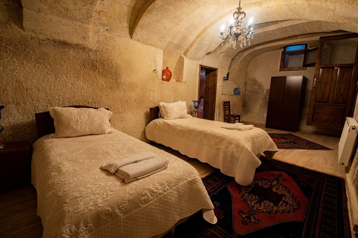 Quarto com duas camas, um candelabro e uma parede de pedra rústica.