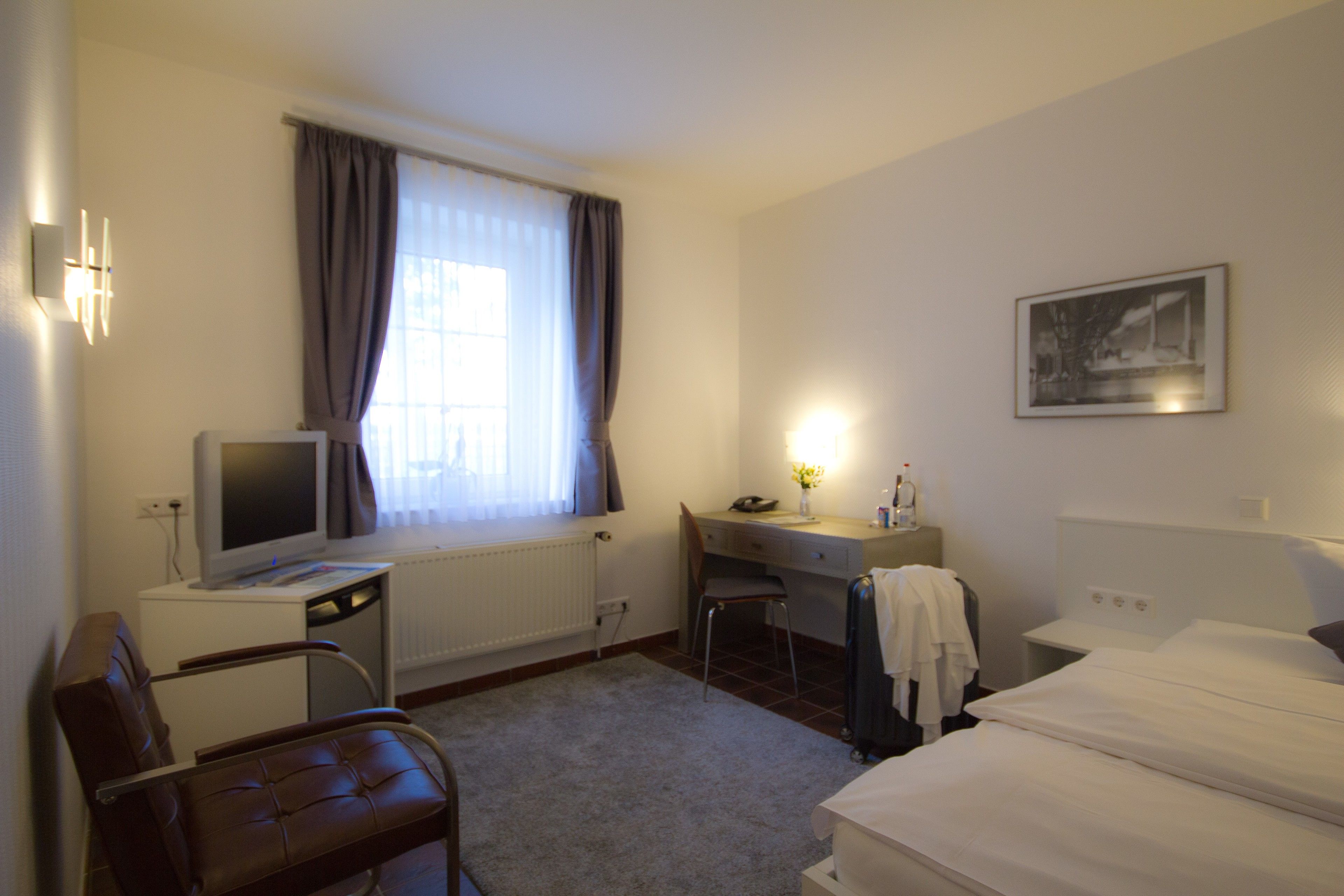 Quarto de hotel com cama, escrivaninha, cadeira e televisão.