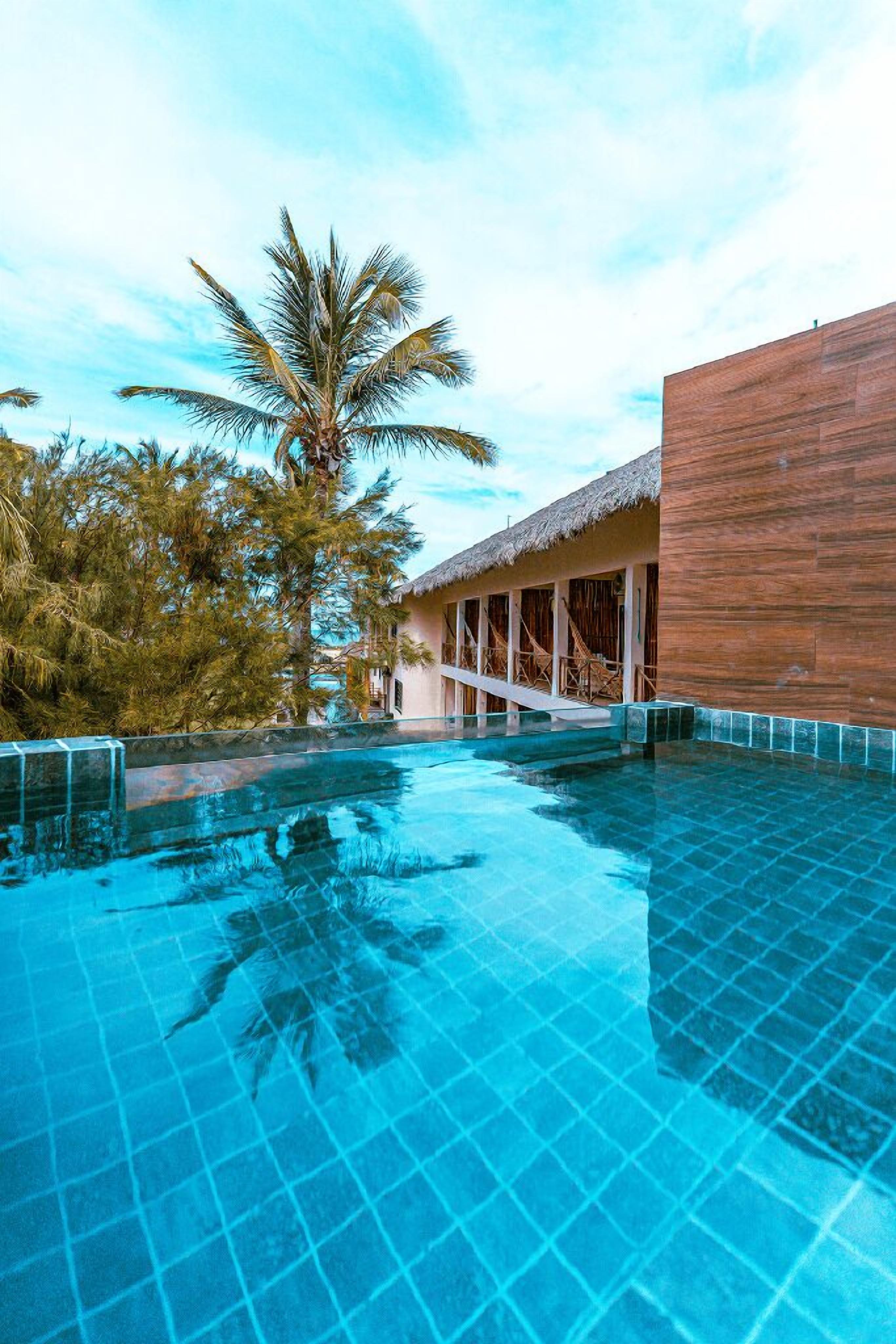 Piscina com água azul cristalina, rodeada por estruturas de madeira e palmeiras.