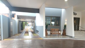 Um hall amplo com piso estampado, um banco de madeira, plantas em vasos e uma escada para um andar superior.