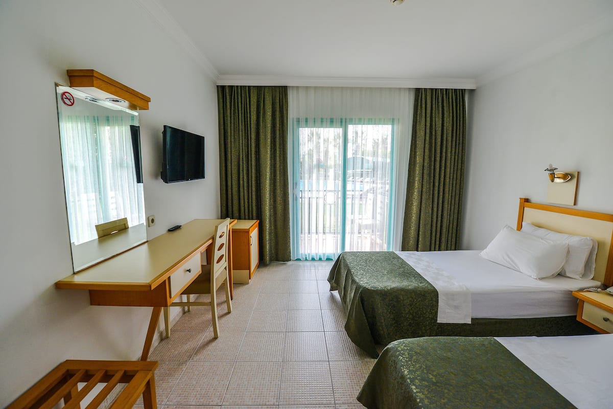 Quarto de hotel com cama, escrivaninha, cadeira, televisão e janela com cortinas.