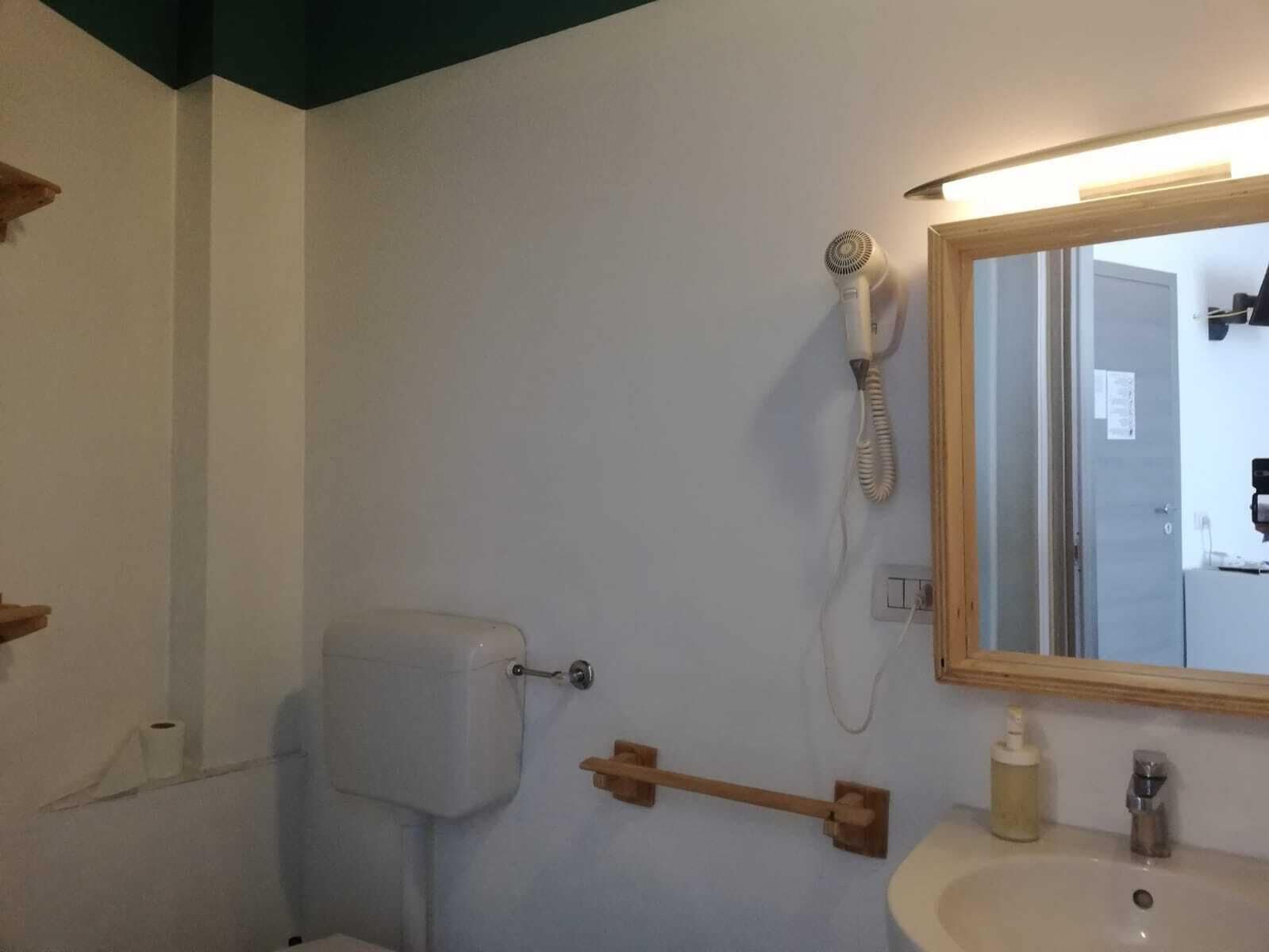 Casa de banho com sanita, lavatório, secador de cabelo e espelho.