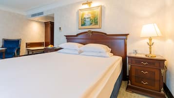 Quarto de hotel com uma cama grande, uma mesa de cabeceira com abajur, uma cadeira e um quadro na parede.