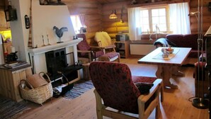 Interior acolhedor de uma cabana com lareira, móveis de madeira, uma mesa de jantar e um gato no teto.