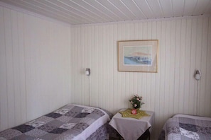 Quarto com duas camas de solteiro, um quadro na parede, uma mesinha com um vaso de flores e uma luminária na parede.