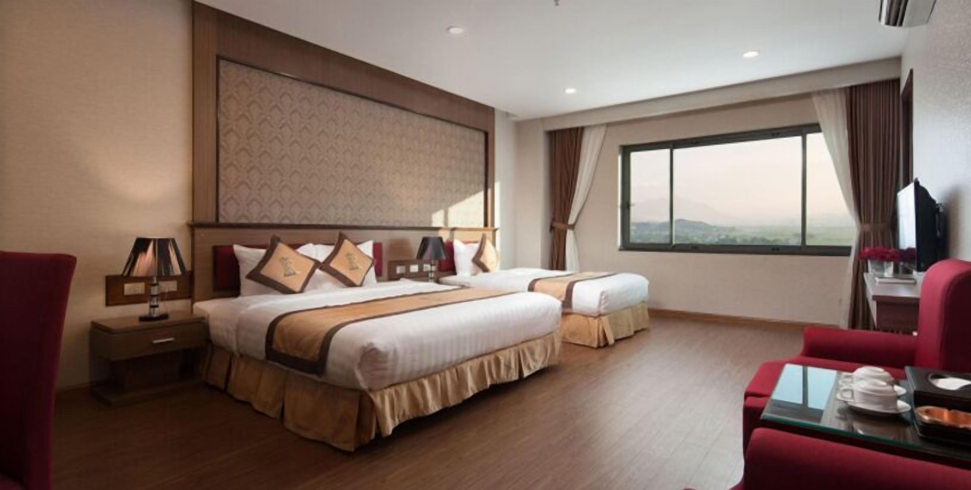 Quarto de hotel com uma cama grande, uma cama menor, uma escrivaninha com cadeira e uma janela ampla com vista.