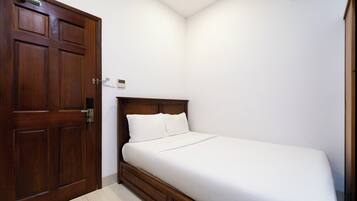 Quarto com porta de madeira, cama com roupa de cama branca e uma pequena mesa de cabeceira.