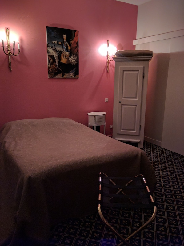 Quarto com cama, mesa de cabeceira pequena, armário e um quadro na parede.