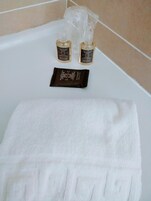 Uma toalha branca, duas embalagens de álcool em gel e um pequeno sachê em uma bancada de banheiro.