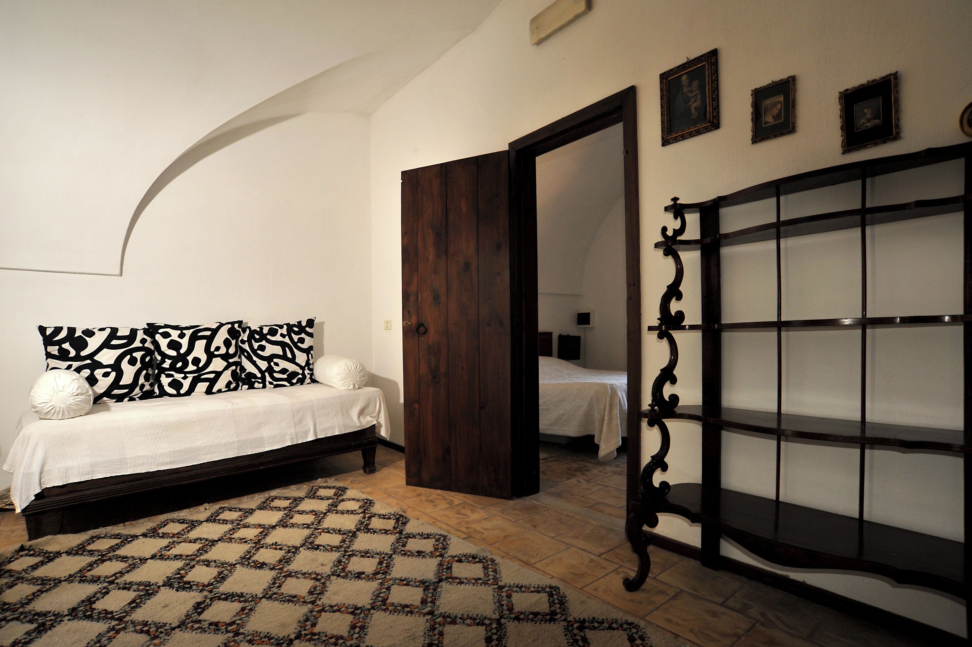 Quarto com cama, guarda-roupa de madeira, tapete estampado e espelho.