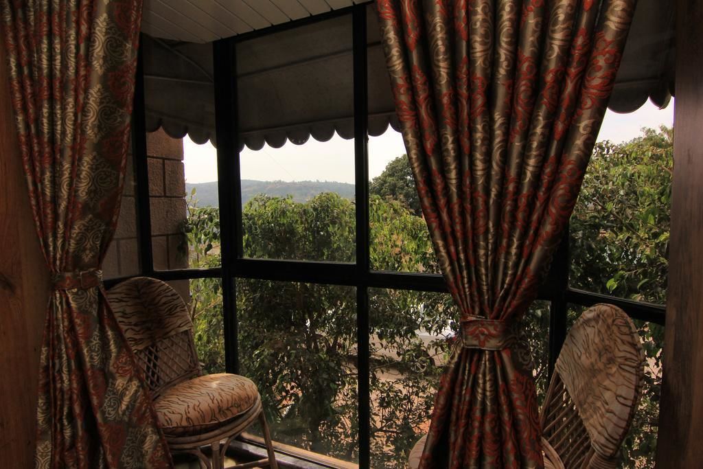 Quarto com vista para uma paisagem exuberante através de amplas janelas, uma cadeira de vime e cortinas estampadas.