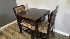 Mesa de jantar com cadeiras, almofada estampada e piso de madeira.