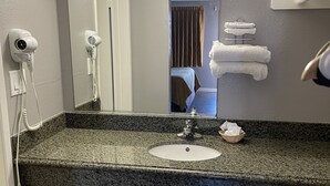 Casa de banho com bancada de granito, lavatório branco, espelho, secador de cabelo e porta-toalhas.