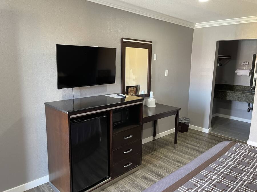 Quarto de hotel com escrivaninha de madeira escura, televisão de tela plana, espelho e lixeira pequena.