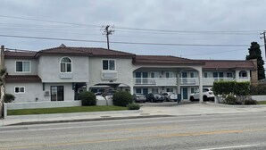 Um motel de dois andares com entrada central, várias varandas e estacionamento com diversos carros.