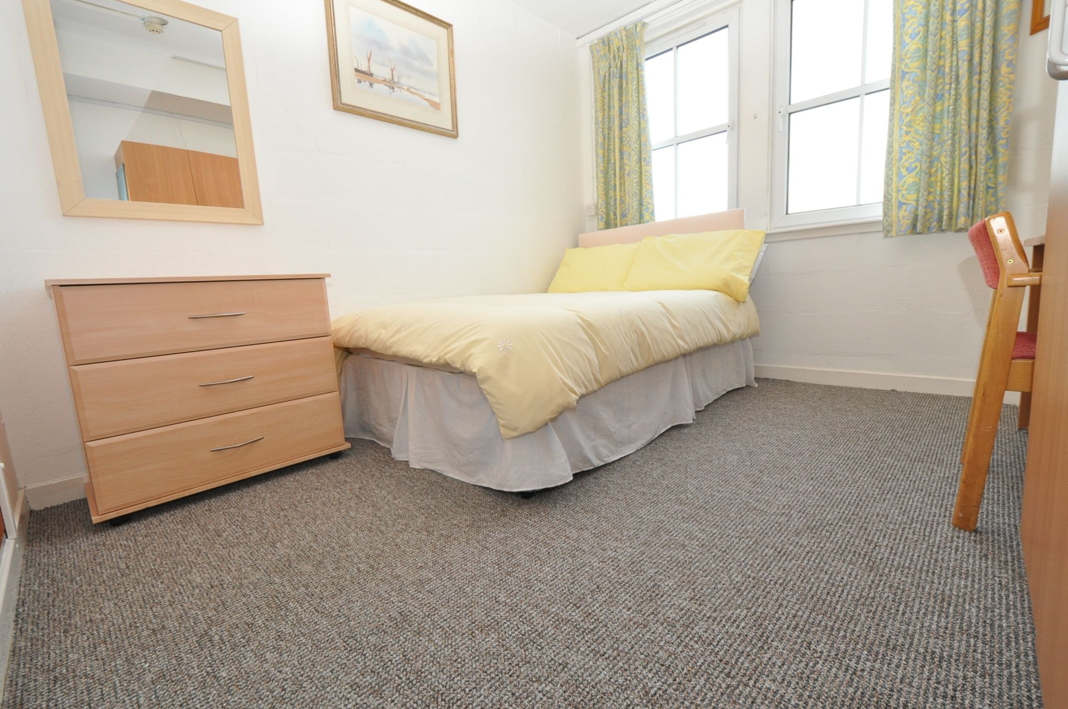 Quarto com cama, penteadeira, espelho e janela com cortinas.