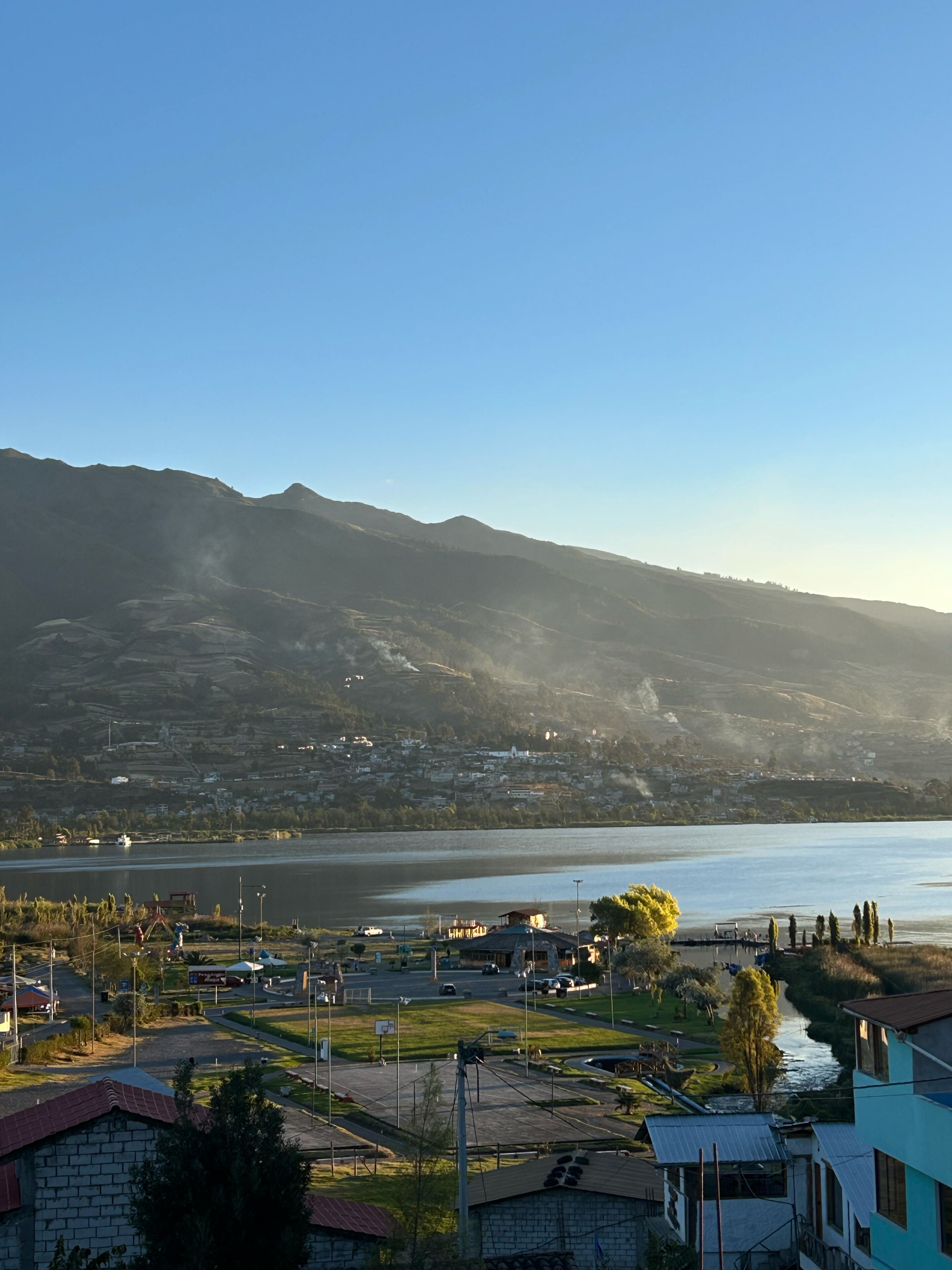 Uma área residencial com um rio, uma ponte e montanhas ao fundo.