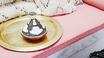 Um banco estofado rosa com uma bandeja de metal decorativa e um recipiente estampado.