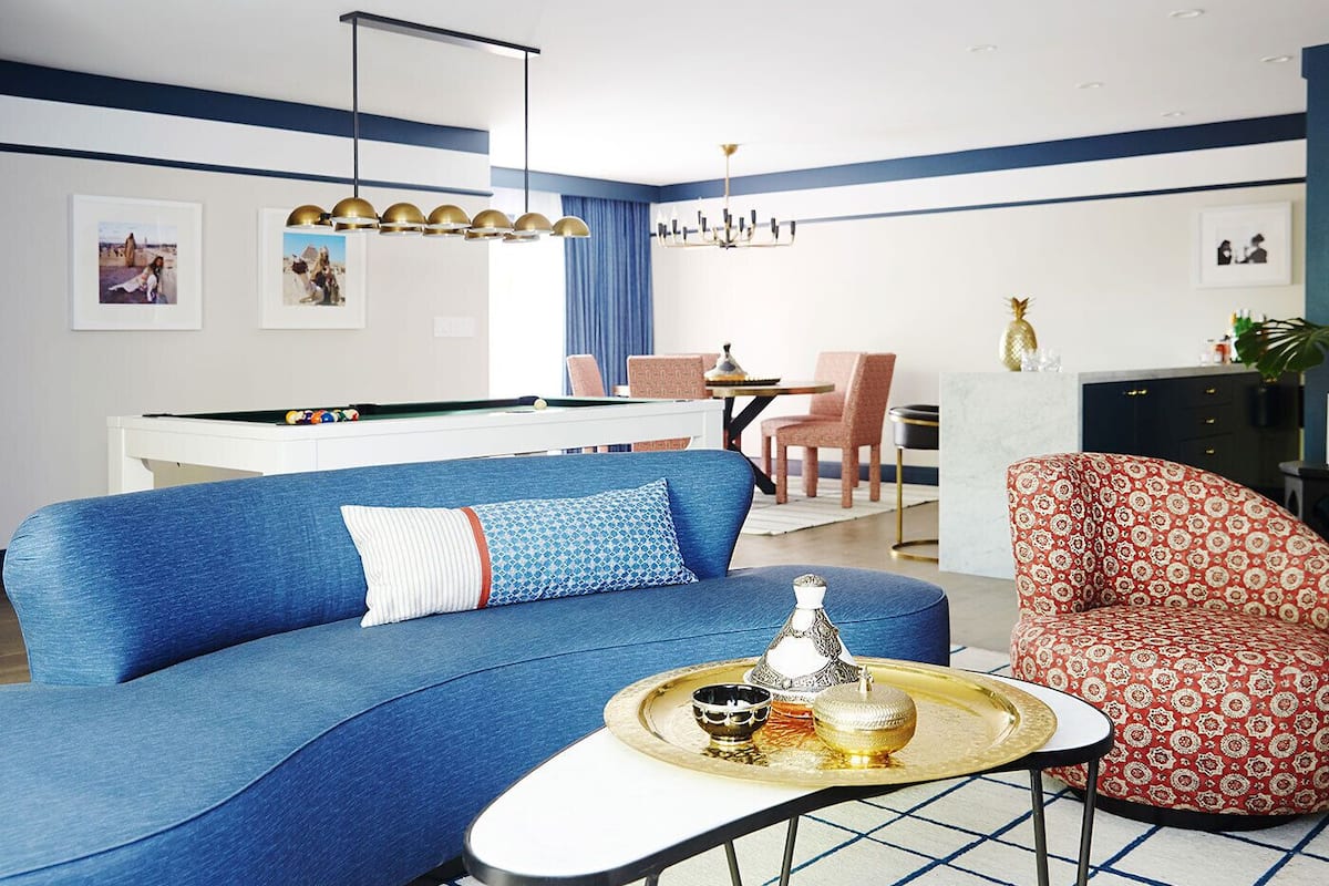 Uma sala de estar moderna com mesa de bilhar, sofá azul e espaço de jantar.