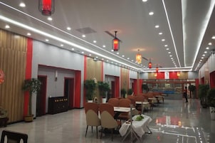 Um saguão de hotel com um balcão de recepção comprido, diversas áreas de estar e um teto alto com iluminação embutida.