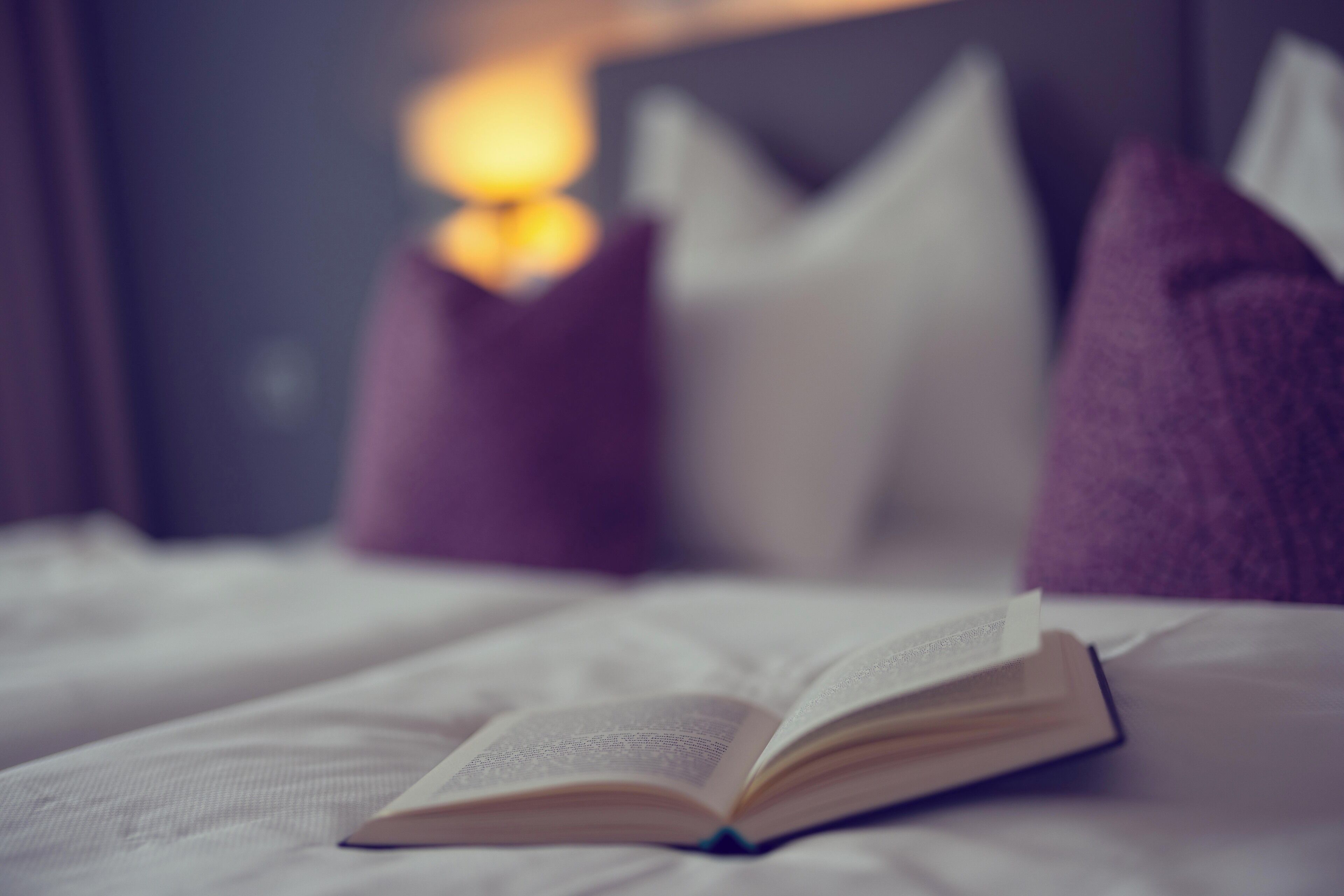 Um livro aberto sobre a cama, com fundo desfocado de almofadas e uma luz suave.