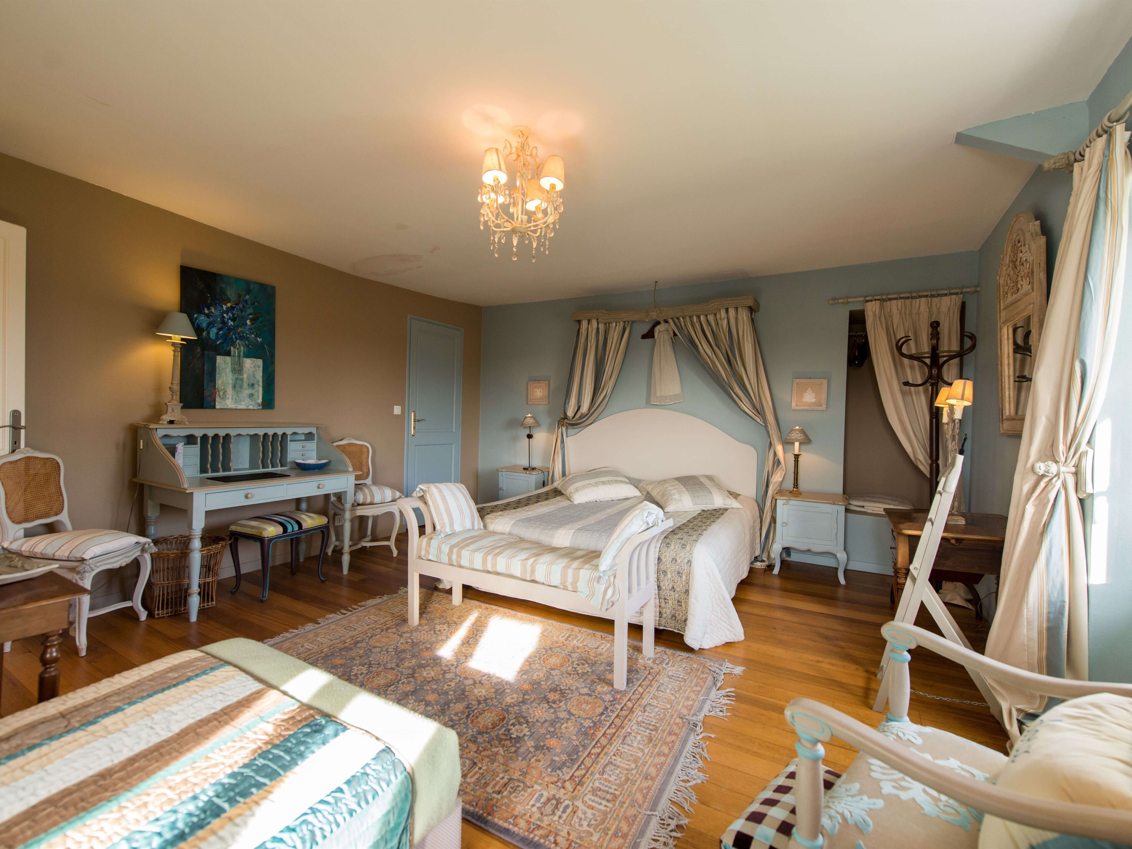Quarto com cama, escrivaninha e cadeira. Um candelabro pendurado no teto.