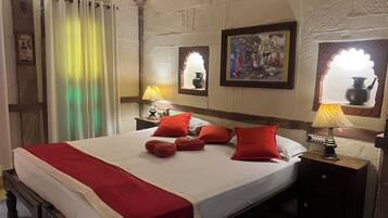 Quarto de hotel com uma cama grande, almofadas vermelhas, cabeceira de madeira, mesa de cabeceira com abajur e um quadro na parede.