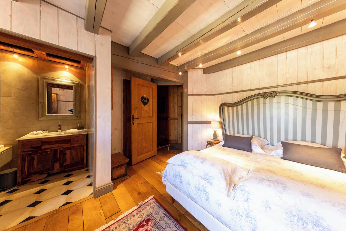Quarto com cama grande, piso de madeira, porta de madeira, espelho e mesa de cabeceira com abajur.