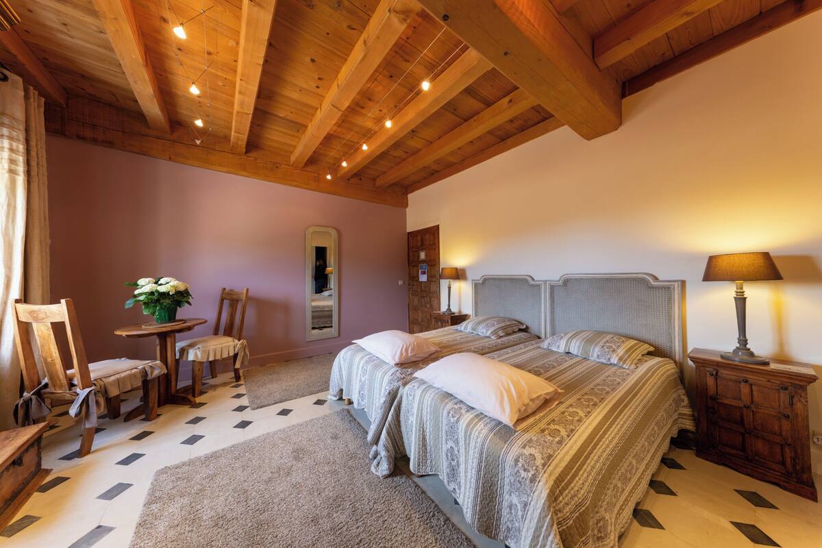 Quarto com duas camas, cabeceiras de madeira, uma mesinha com cadeiras e um espelho na parede.