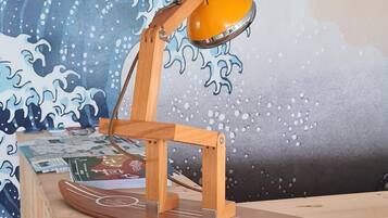 Uma escrivaninha de madeira com uma luminária amarela, base em formato de prancha de surf e parede ao fundo com padrão de ondas.