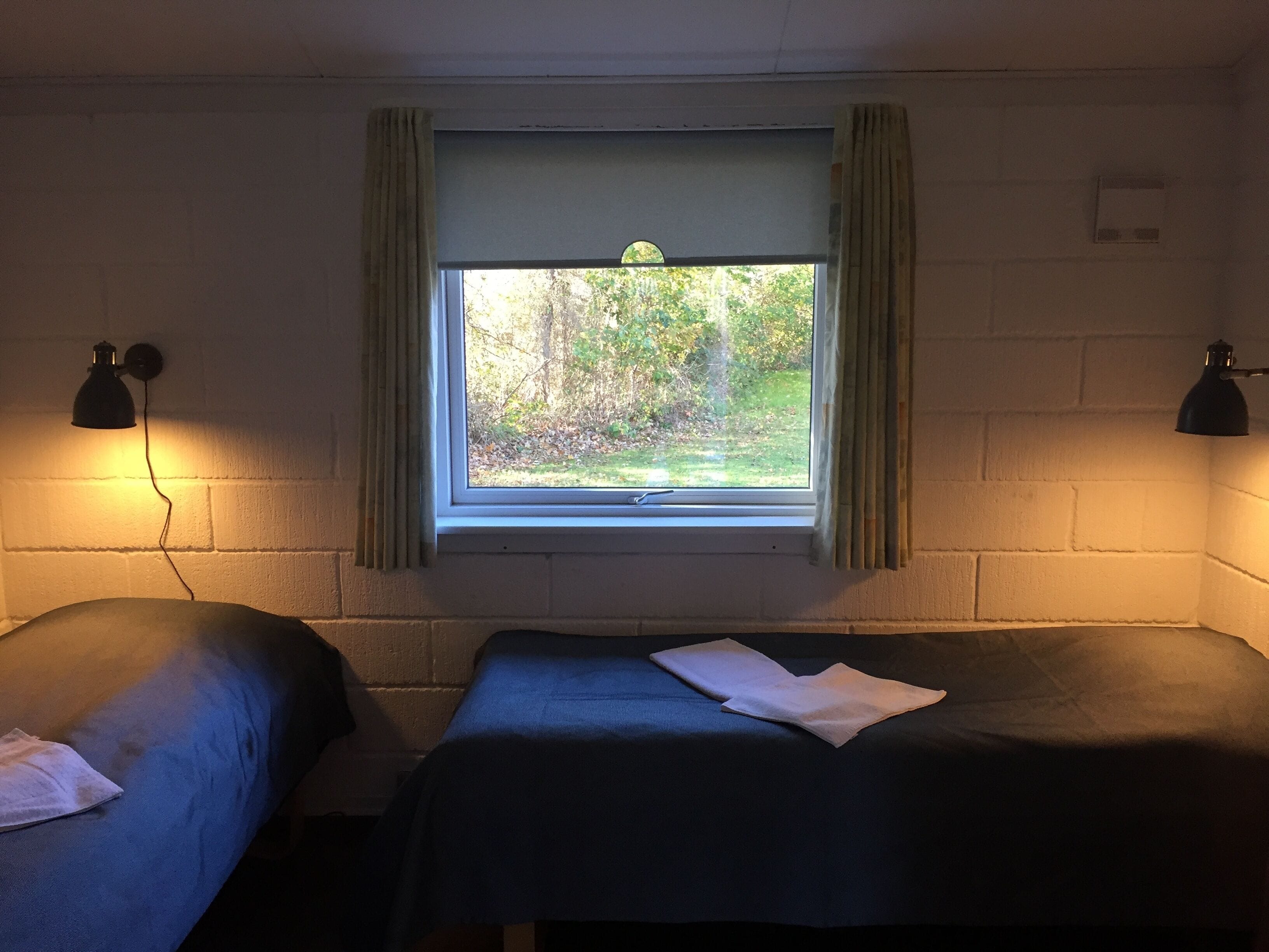 Quarto com duas camas, janela com cortinas e luminárias na parede.